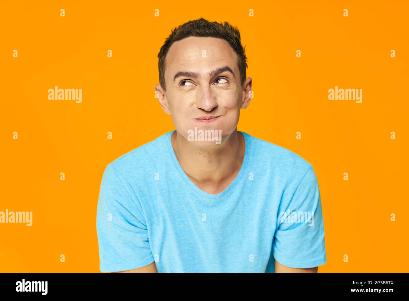 Cheerful man puffed out his cheeks and looks up on a yellow background ...