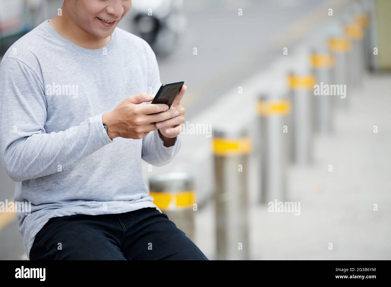 Close-up of smiling young Asian man in gray sweater sitting on metal ...