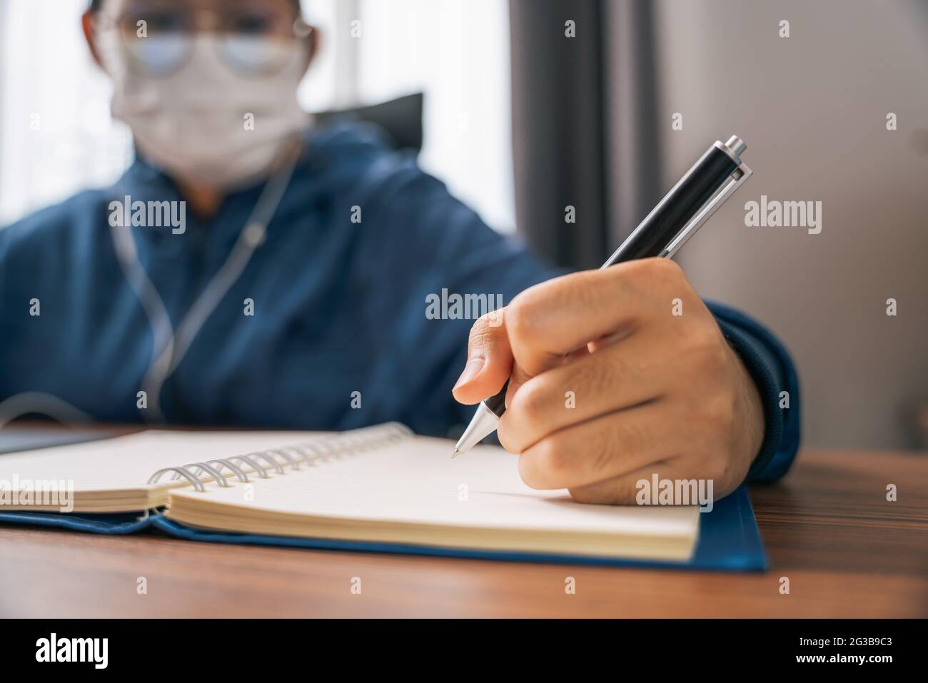 Close up hand of young girl wear a mask writing note on a book looking ...
