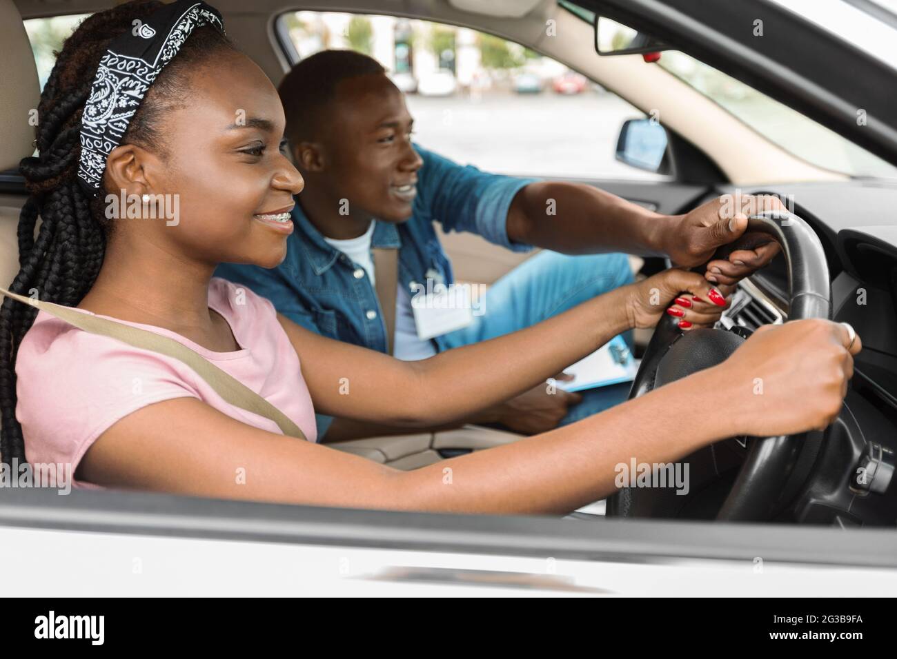 Smiling young black woman practicing parking at driving school, sitting ...