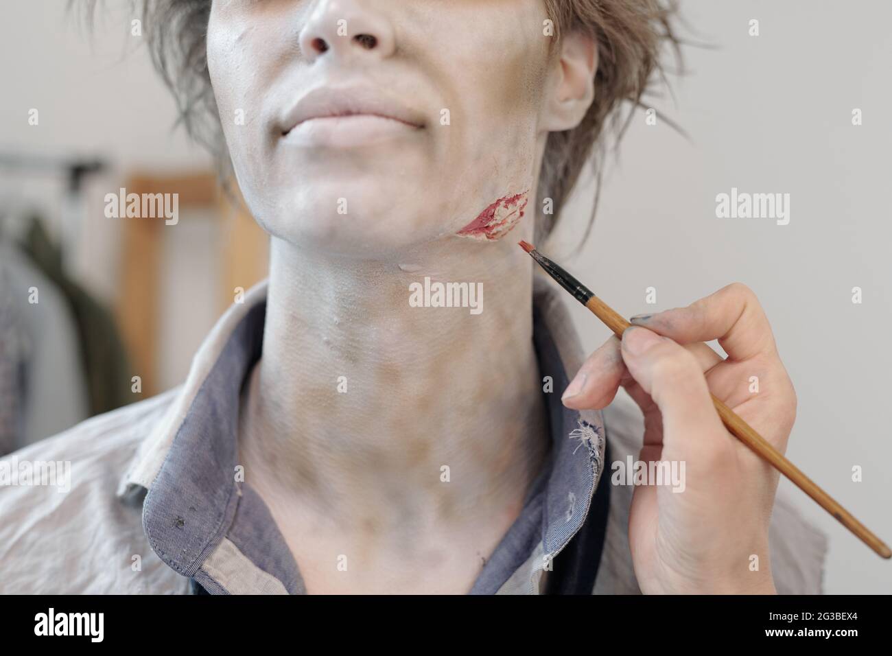 Hand of makeup artist with paintbrush making zombie visage on face of ...