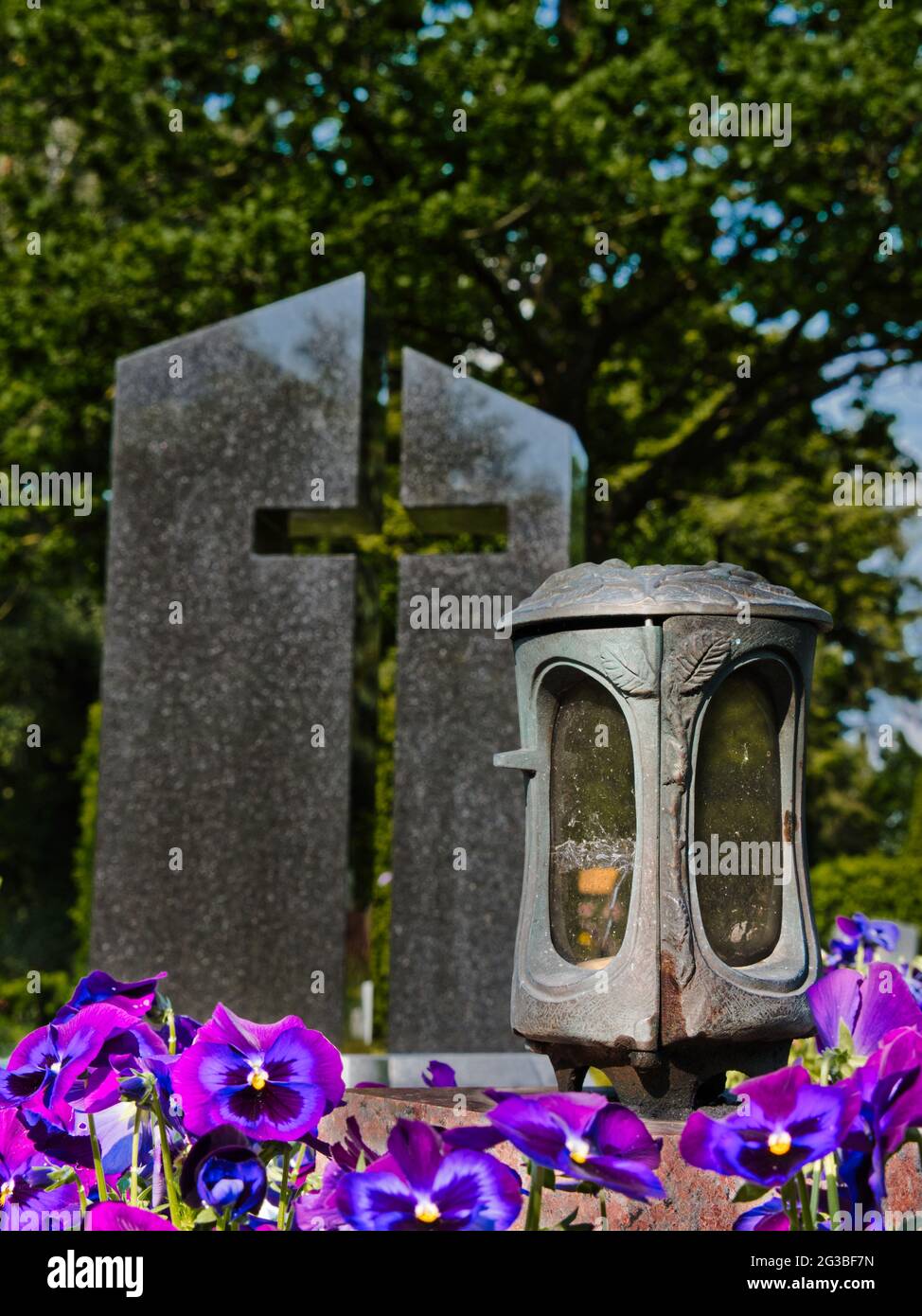 A lantern in front of a blurred Christian tombstone with purple flowers ...