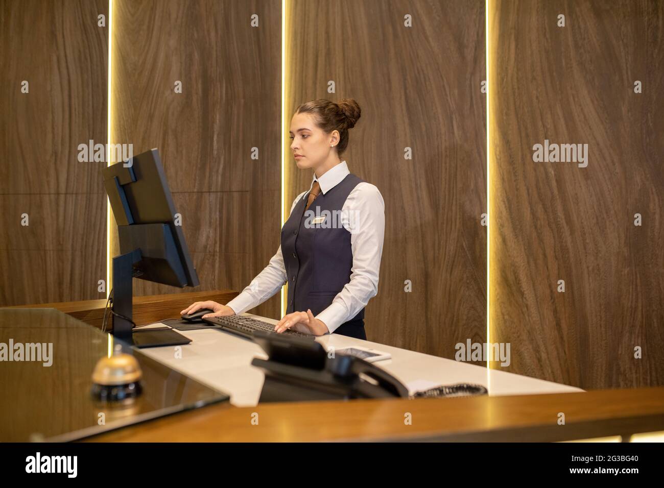 Young receptionist in uniform using computer by counter Stock Photo - Alamy