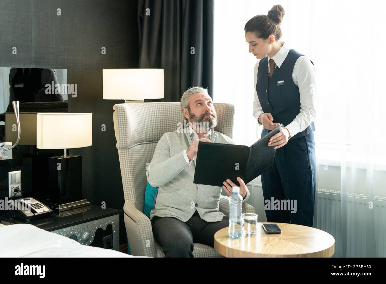 Young hotel manager offering menu to mature businessman Stock Photo - Alamy