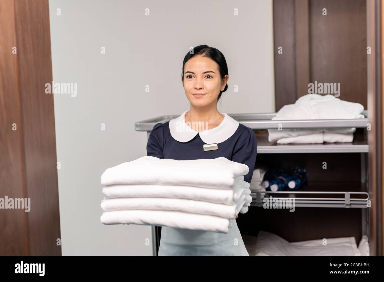 Pretty room service staff holding clean sheets while standing by open ...