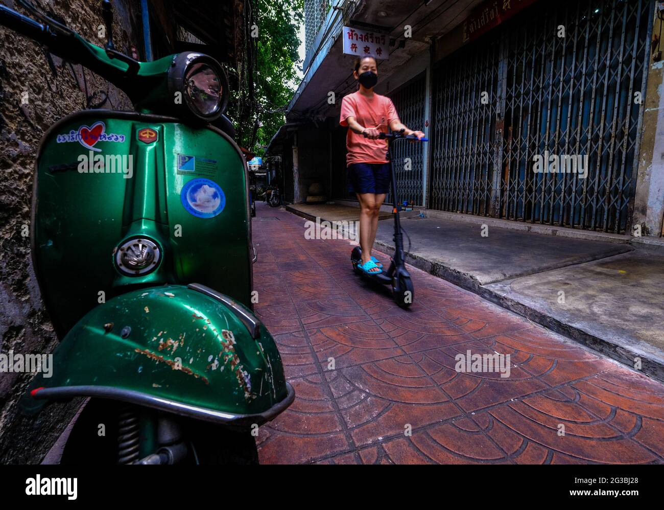 iA young woman rides a scooter down a narrow alley in Chinatown ...