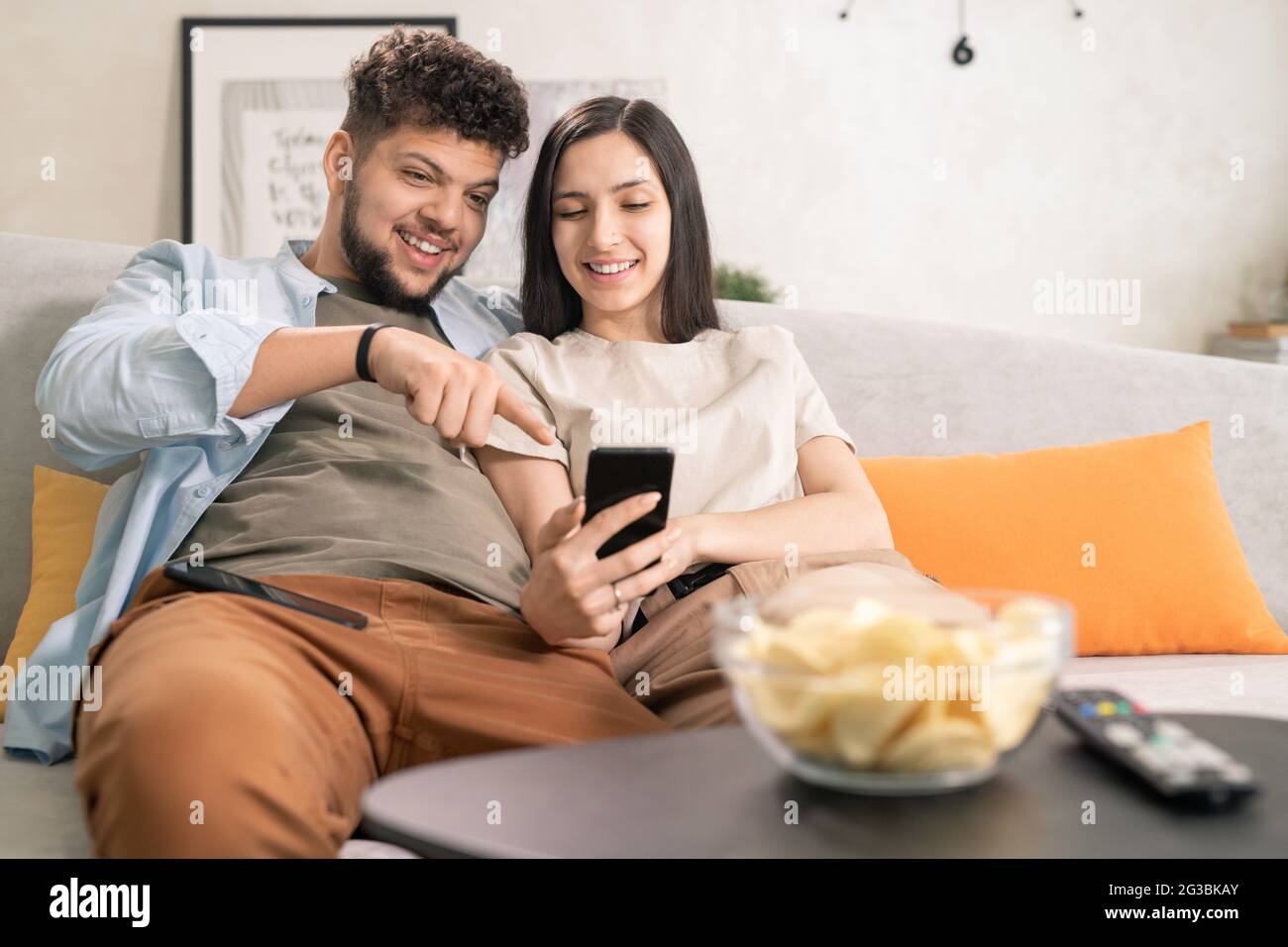 Young joyful man pointing at screen of smartphone held by his wife ...