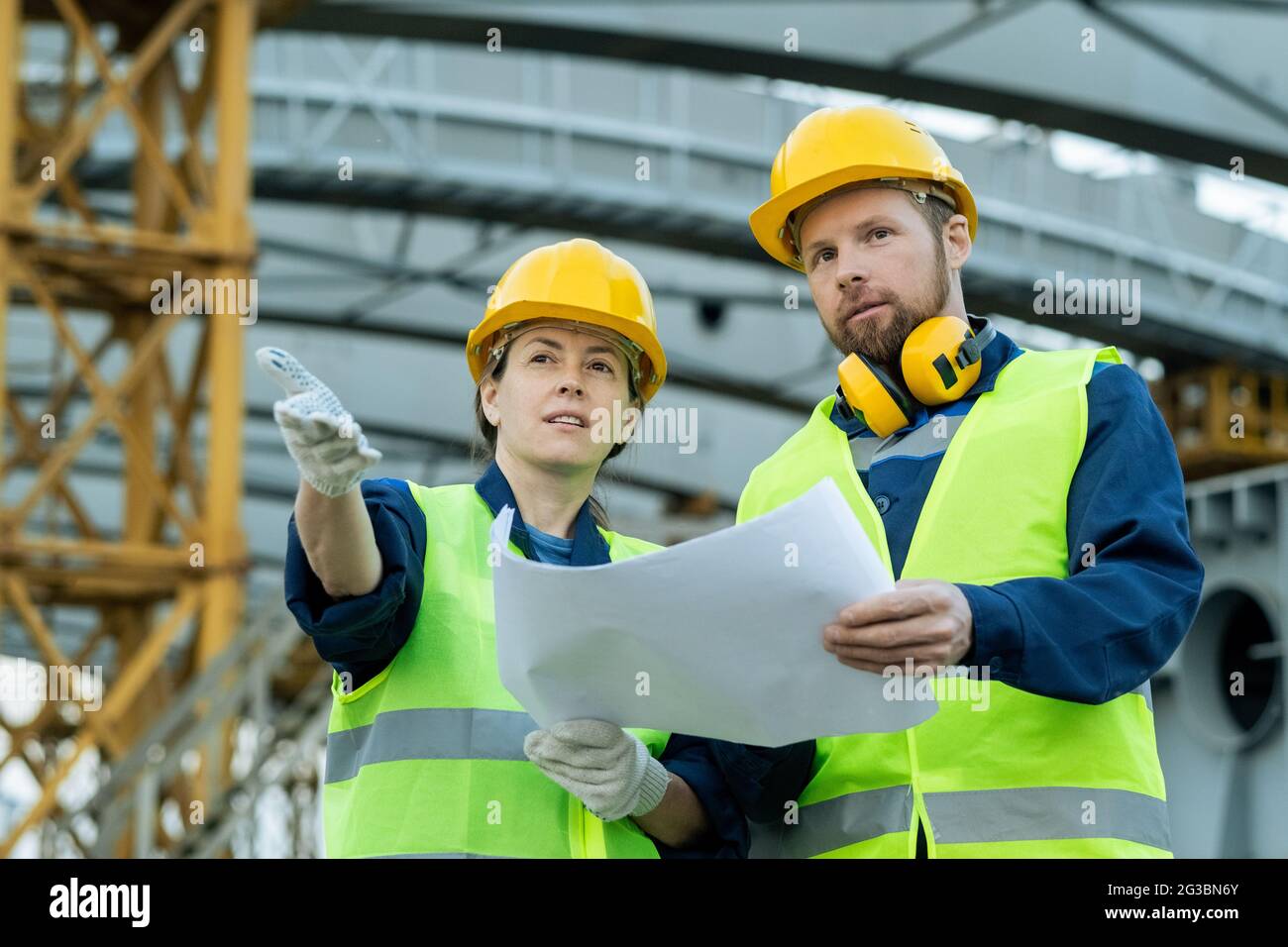 Two confident builders with blueprint discussing construction site ...