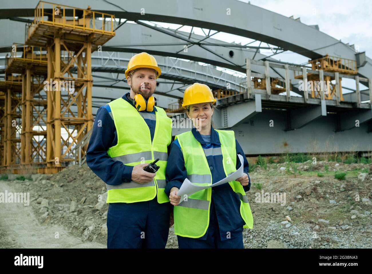 Two successful engineers in workwear standing against large ...