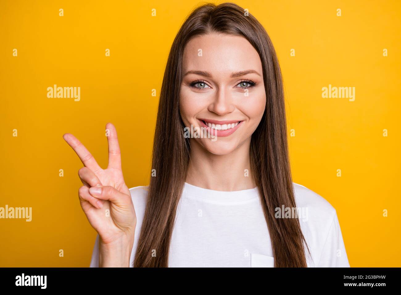 Photo portrait of smiling woman showing v-sign isolated on vivid yellow ...