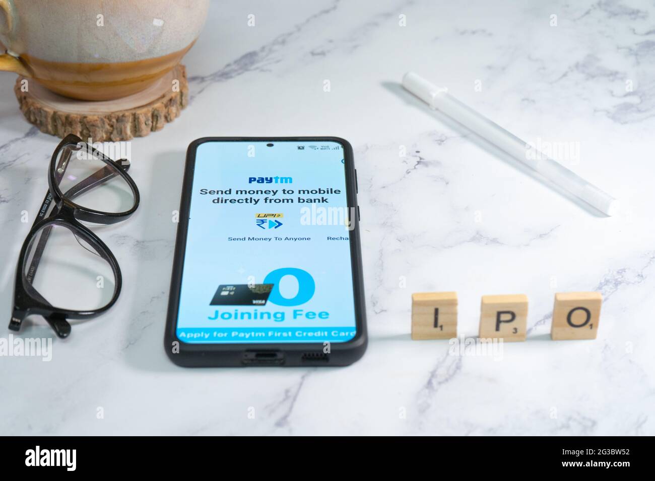 paytm logo screen on mobile phone with pen and spectacles placed nearby ...