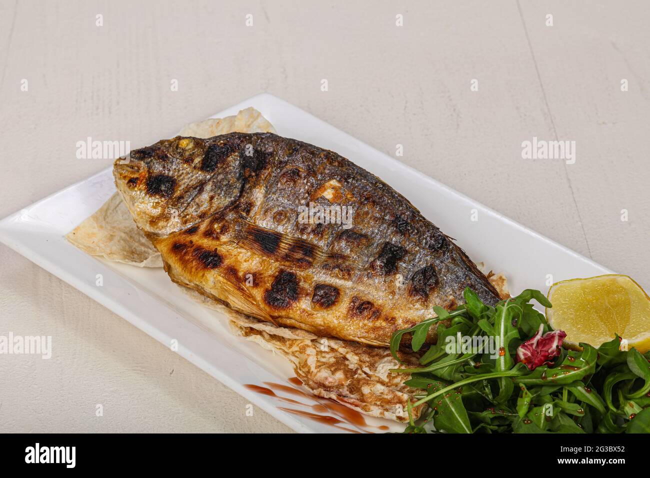 Grilled dorada fish served lemon and rucola Stock Photo - Alamy