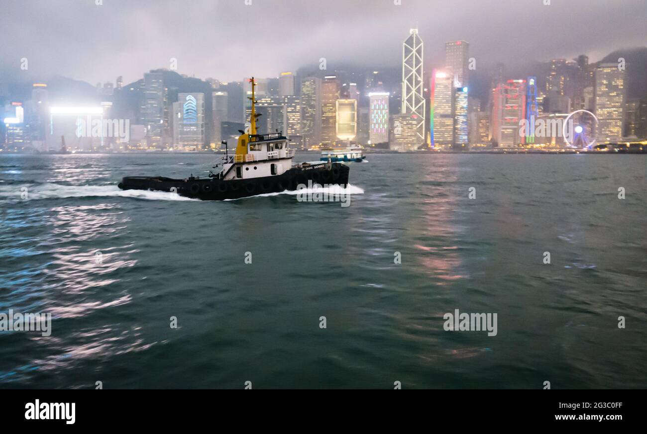Tug boat in Hong Kong harbour in the early evening with city backdrop ...