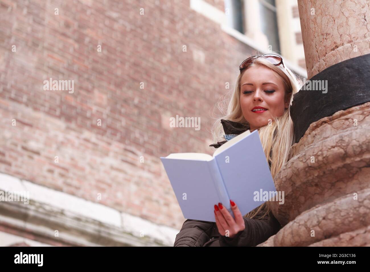 Low angle view of a pretty blond woman reading a book outdoors in town ...