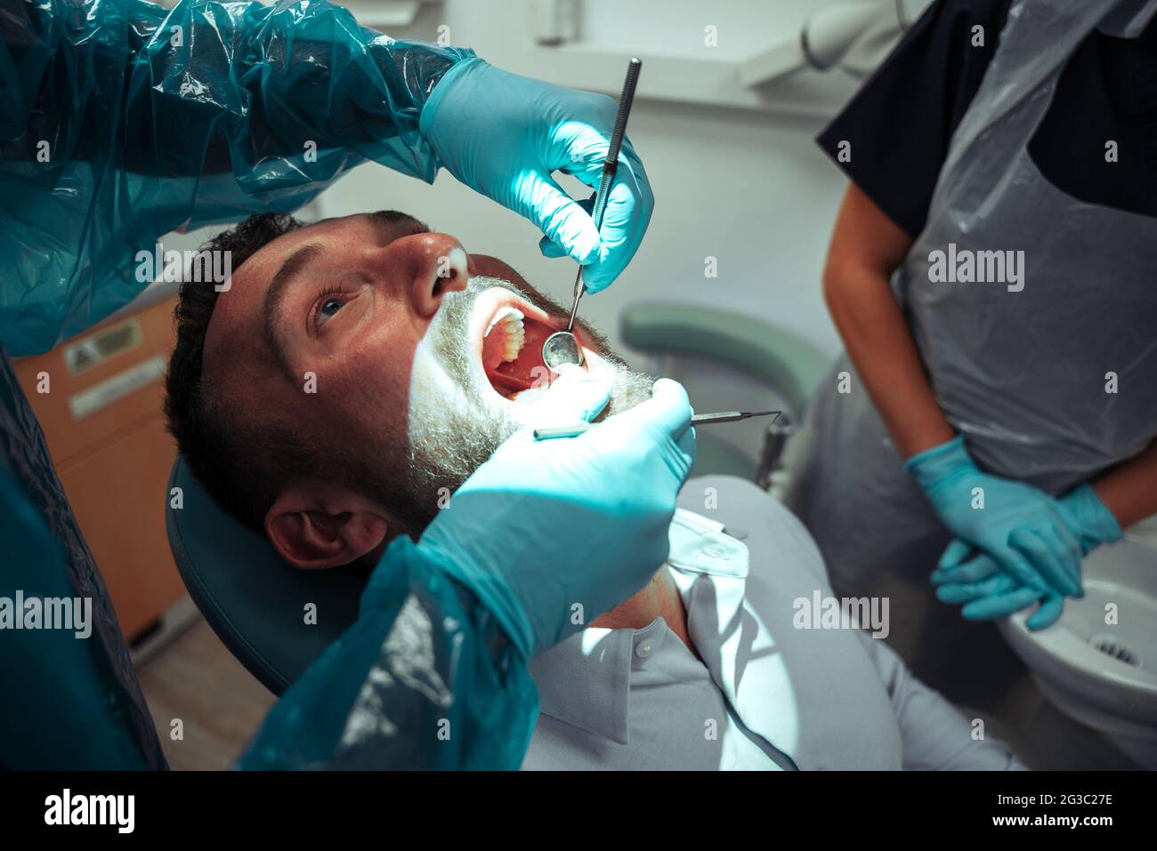 Caucasian male sitting with mouth wide open while male dentist cleans ...