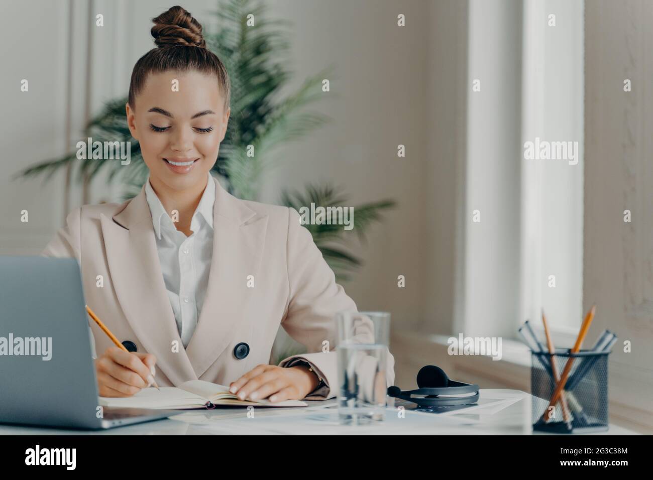 Young successful businesswoman in formal wear writing down information ...