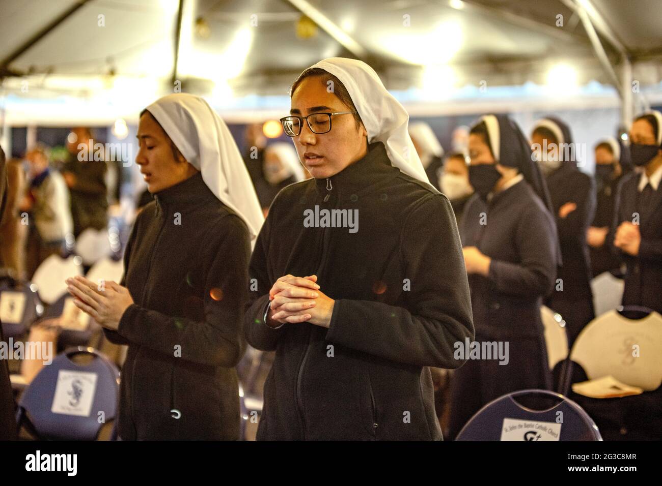 Multiracial nuns in habit pray at an outdoor mass in a tent for ...