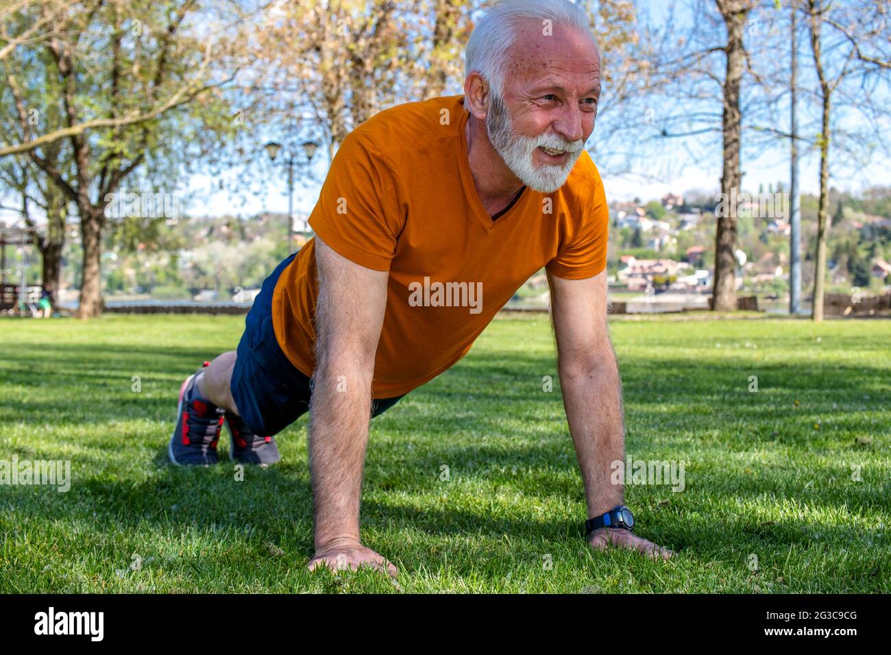 Portrait of a senior man exercising, doing push ups in the park. An ...