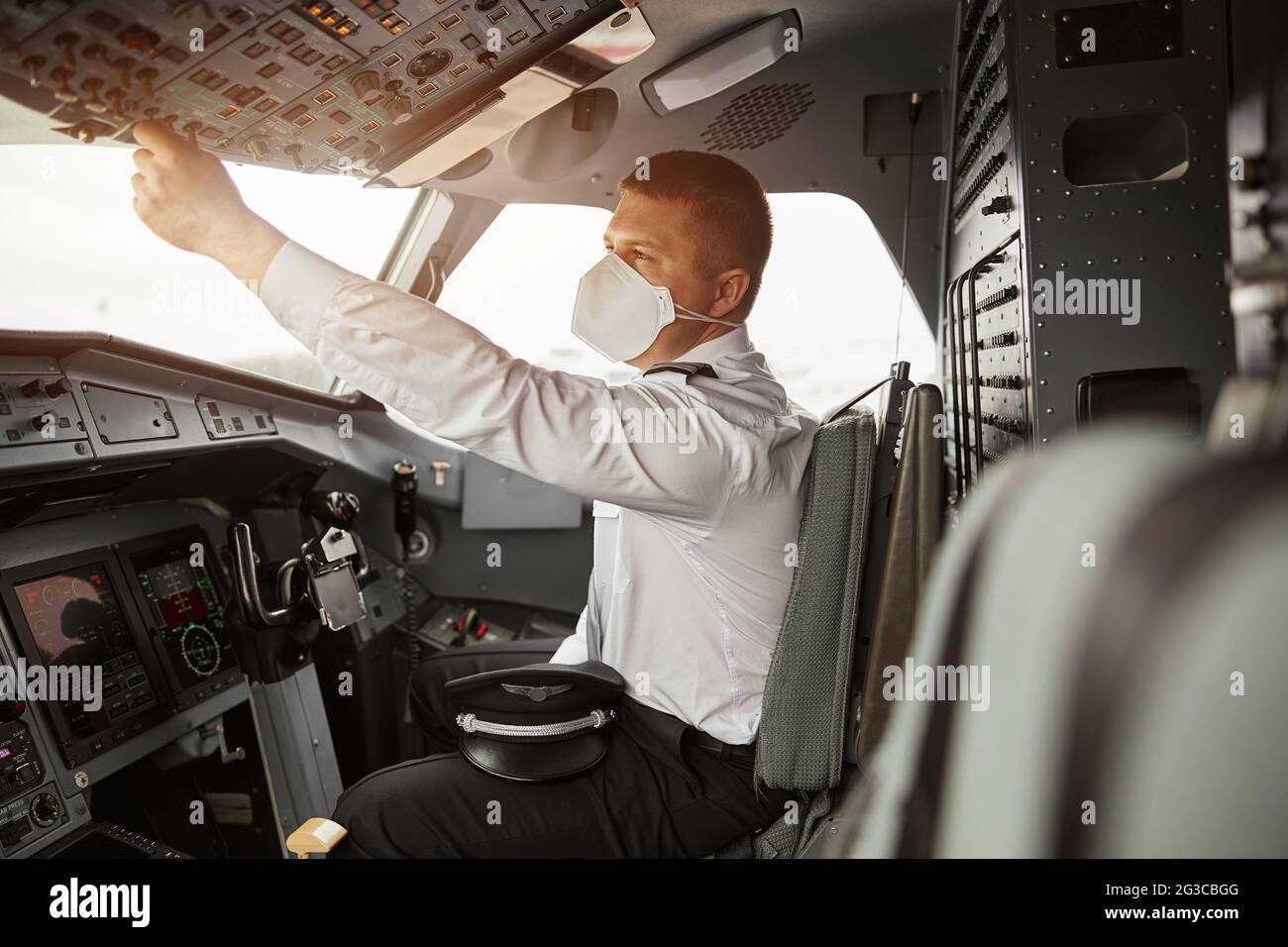 Male pilot turning button on passenger airplane Stock Photo - Alamy