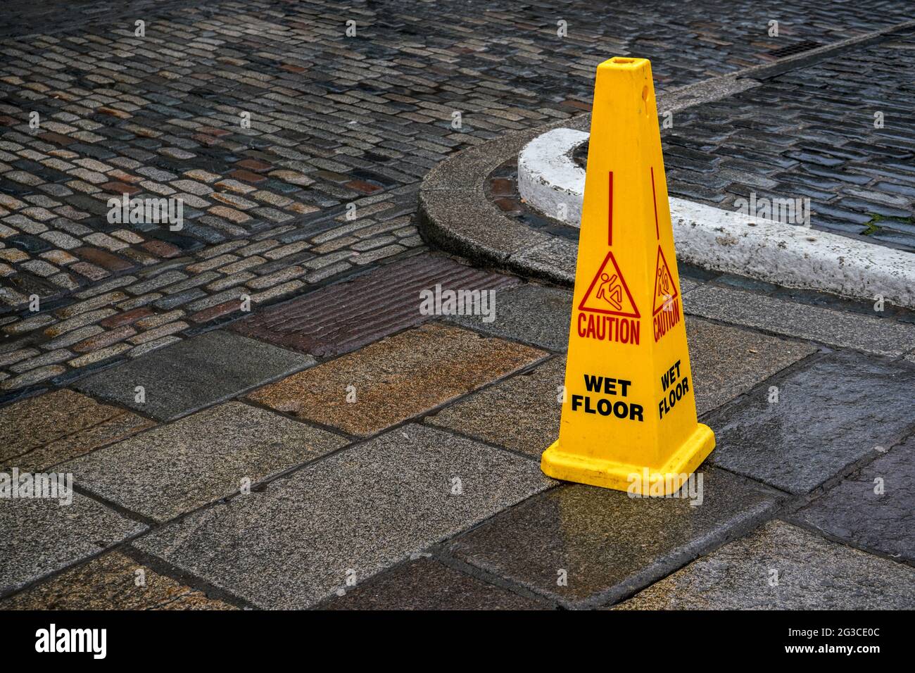Yellow cone with caution slippery surface sign, on wet stone tiles ...