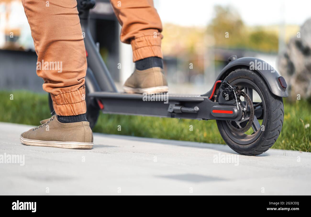 Man feet on electric scooter, closeup detail, sun lit blurred grass in ...