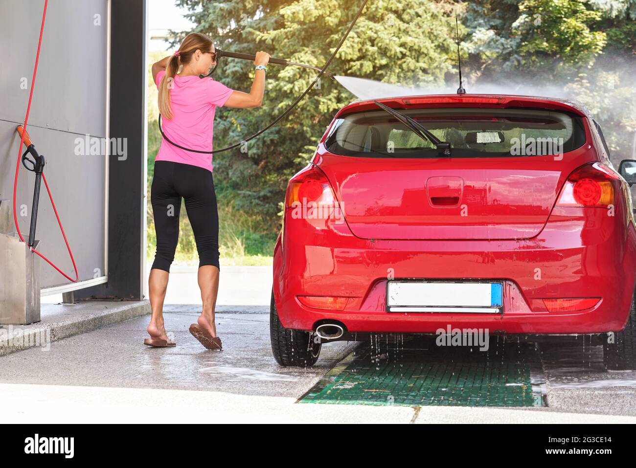 Young woman washing her red car in self serve carwash, view from back ...