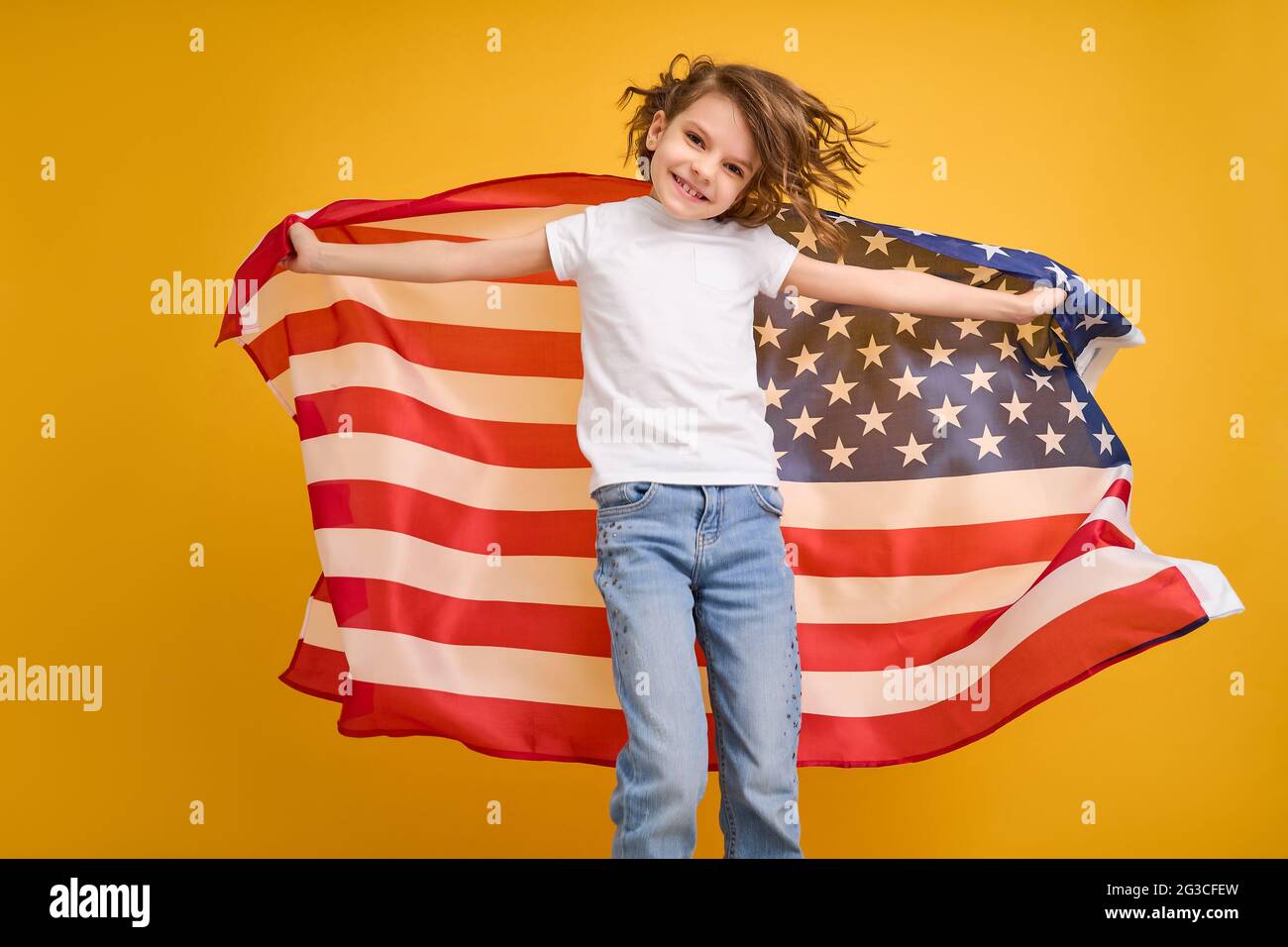 Happy child, cute girl with American flag on yellow studio background ...