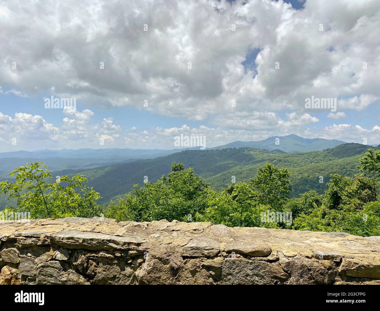 View of mountains, trees and clouds as seen from a man-made stone ledge ...