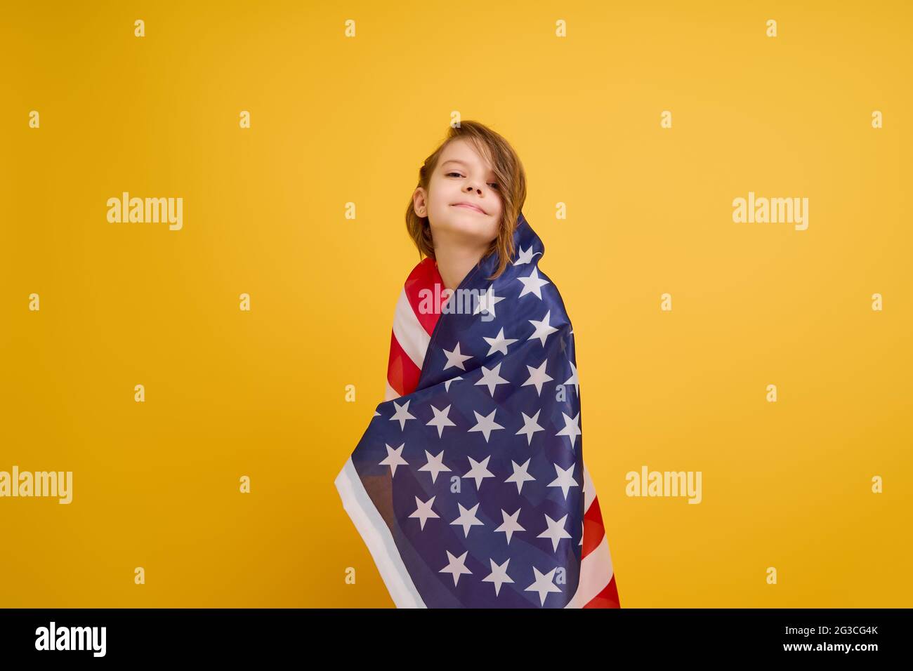 Happy child, cute girl with American flag on yellow studio background ...