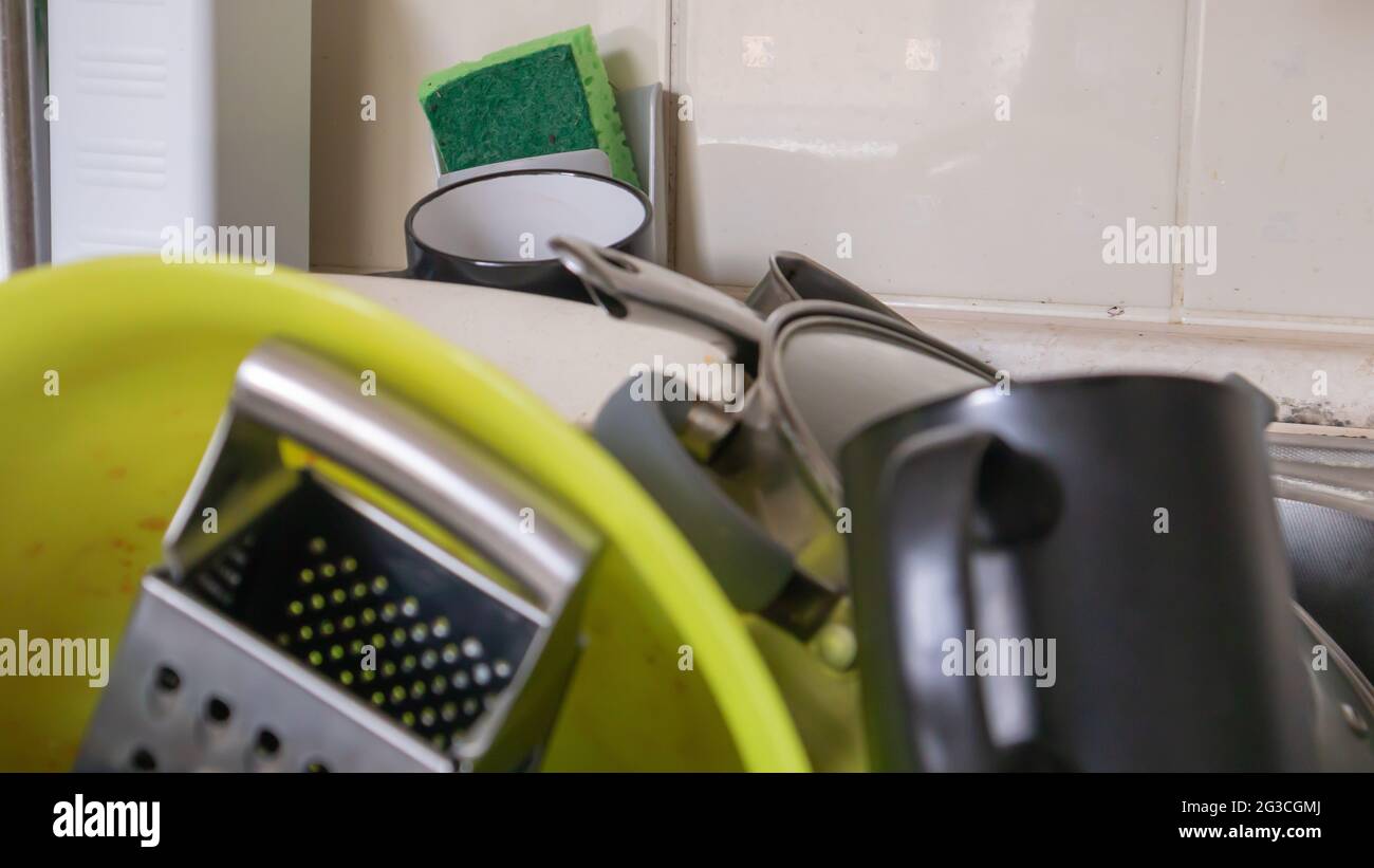 The kitchen utensils in the wash basin need to be washed. A pile of ...
