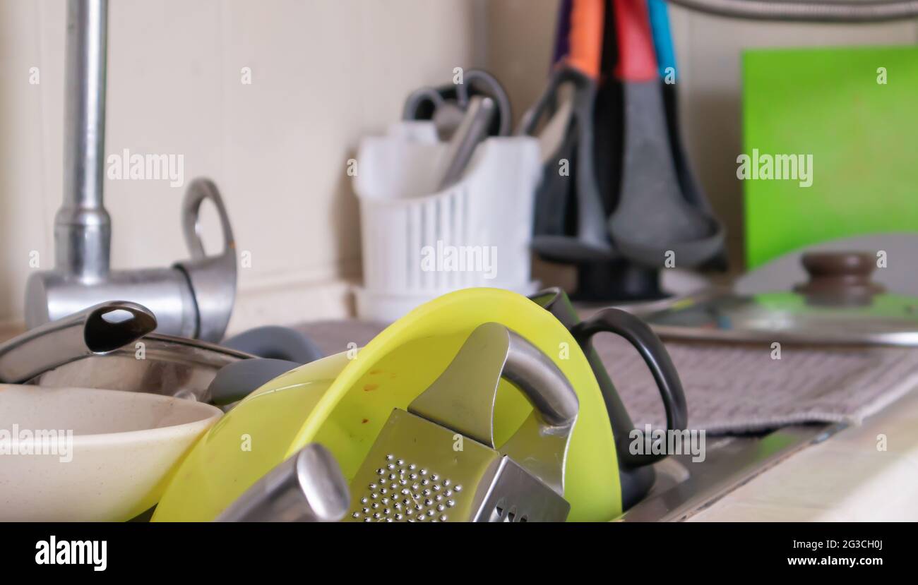 The kitchen utensils in the wash basin need to be washed. A pile of ...