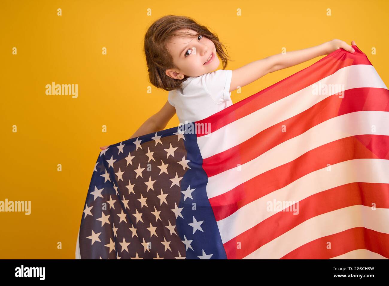 Happy child, cute girl with American flag on yellow studio background ...
