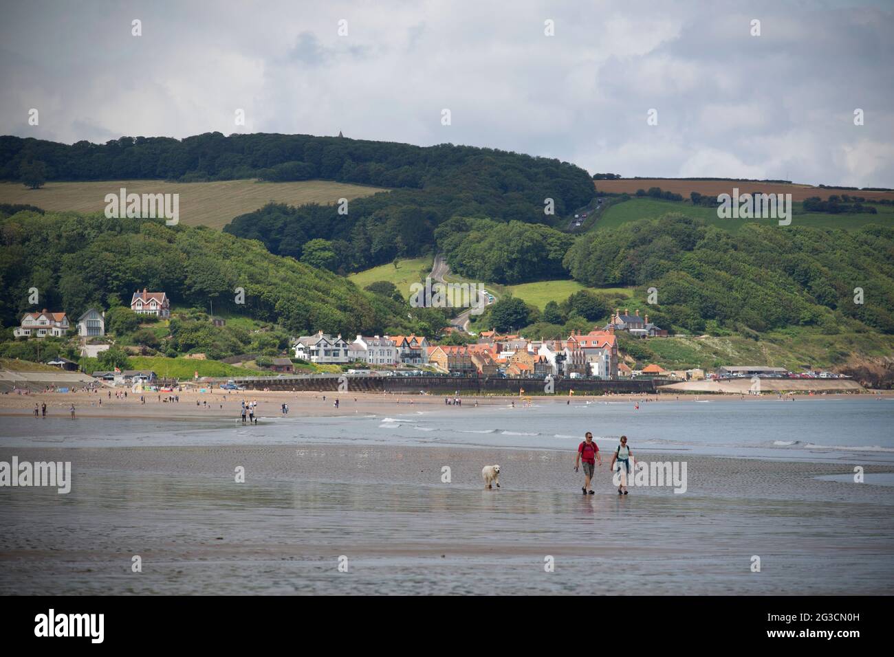 People stroll along Sandsend beach with the small fishing town of ...