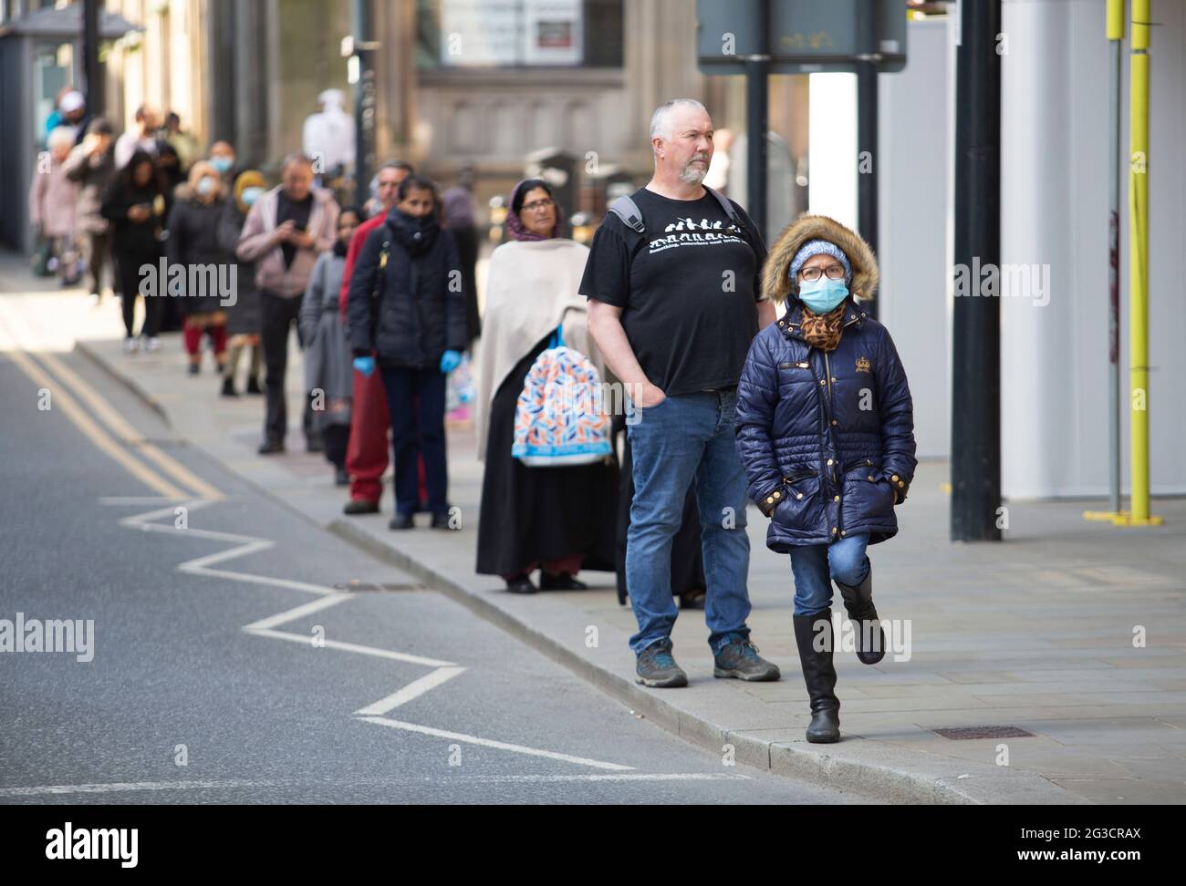 A woman wearing a protective face mask in a long queque outside ...
