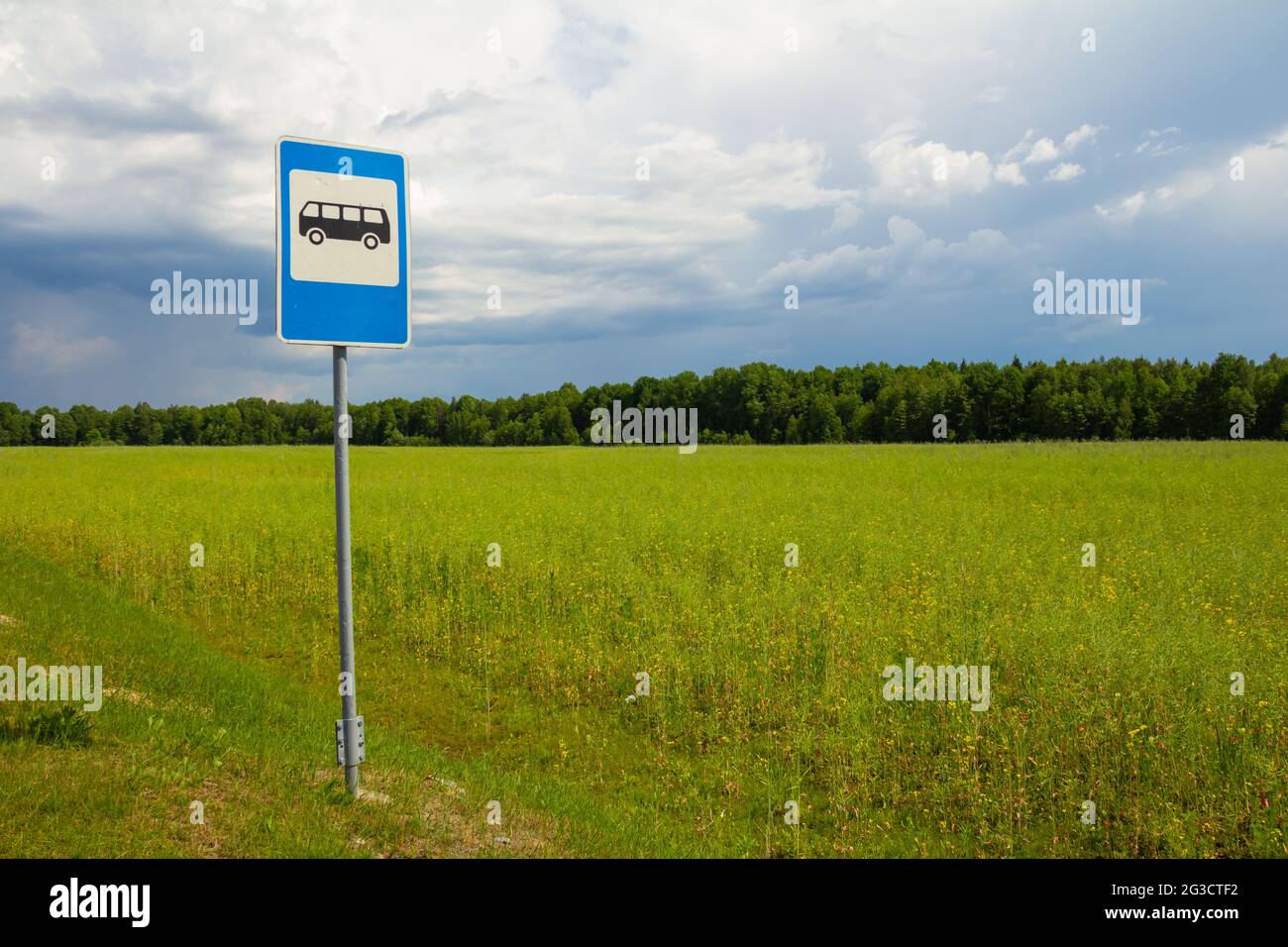 Bus stop sign on a background of blue cloudy sky, green field and ...