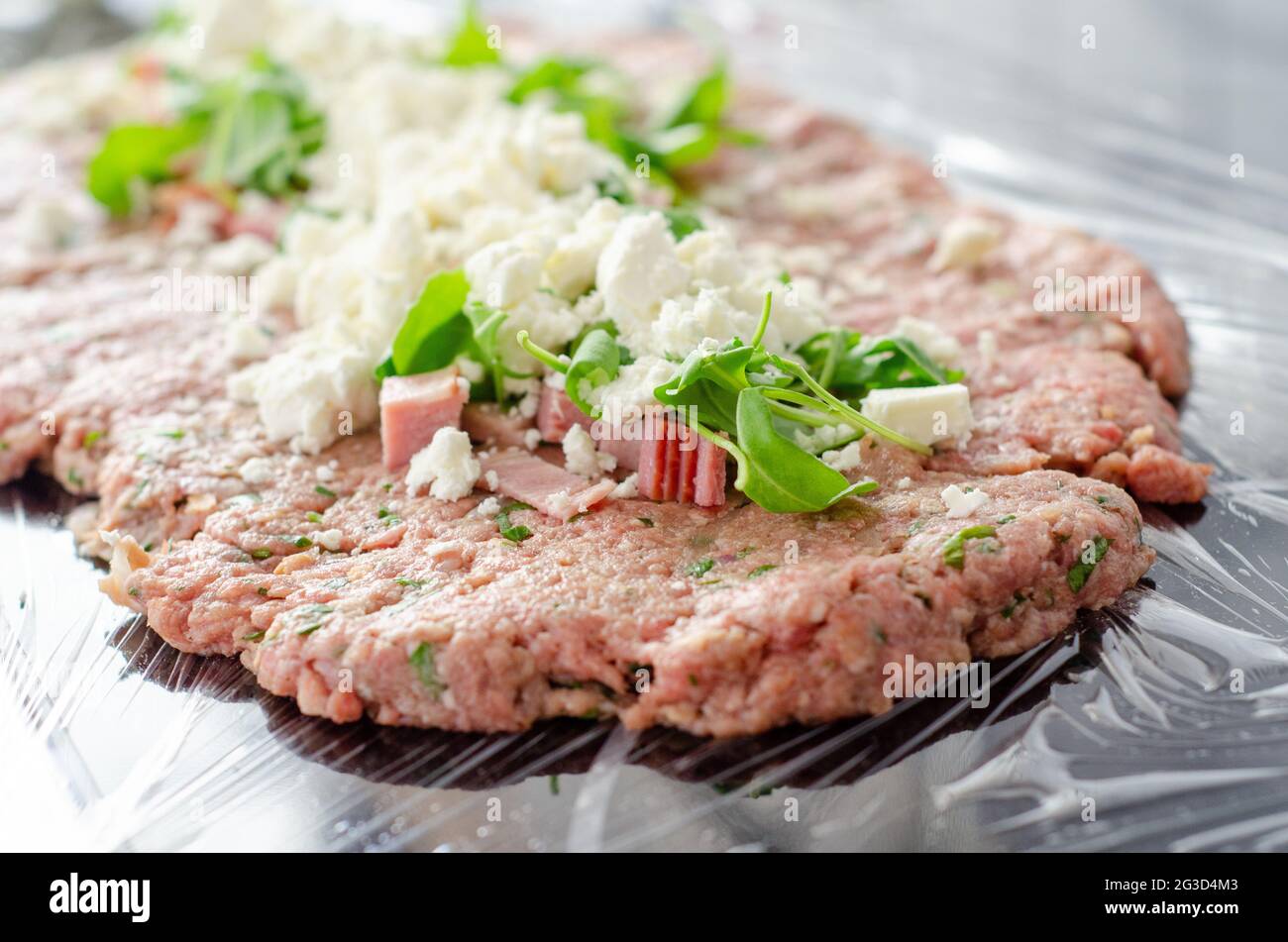 Ground meat with chopped greens and cheese laid out on a cling film for ...