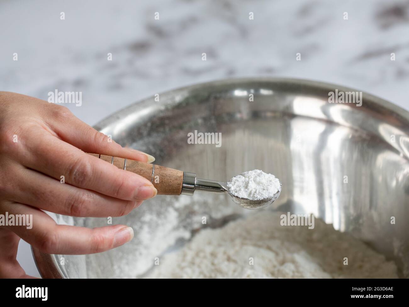 hand holding a measuring spoon with white powder in a metal round ...