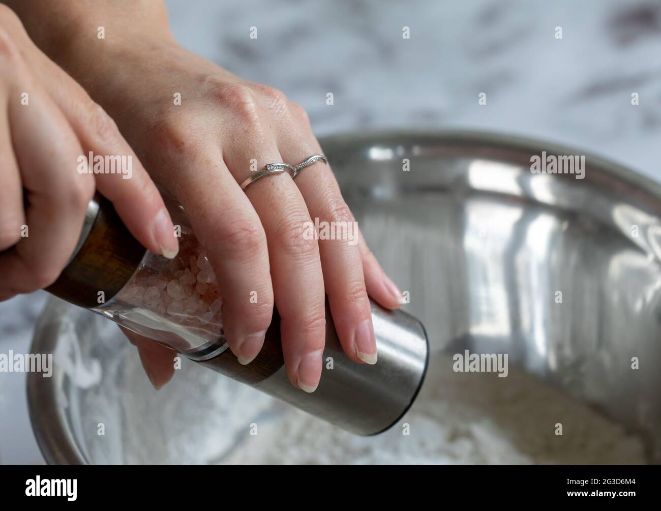 Close up of a woman's hands holding a salt grinder over a metal mixing ...