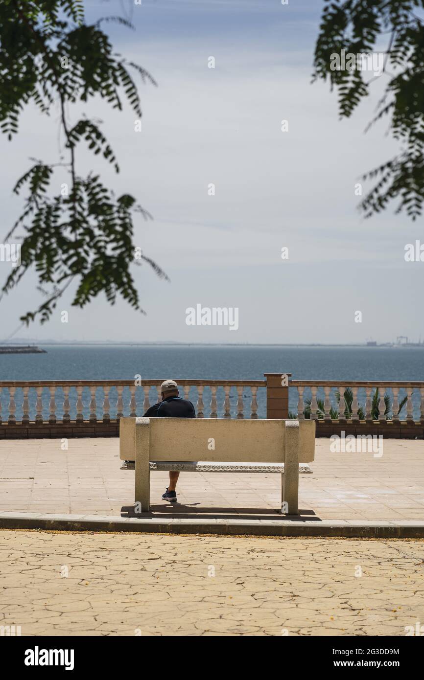 Lonely old man sitting on a stone bench in a sunny park overlooking the ...