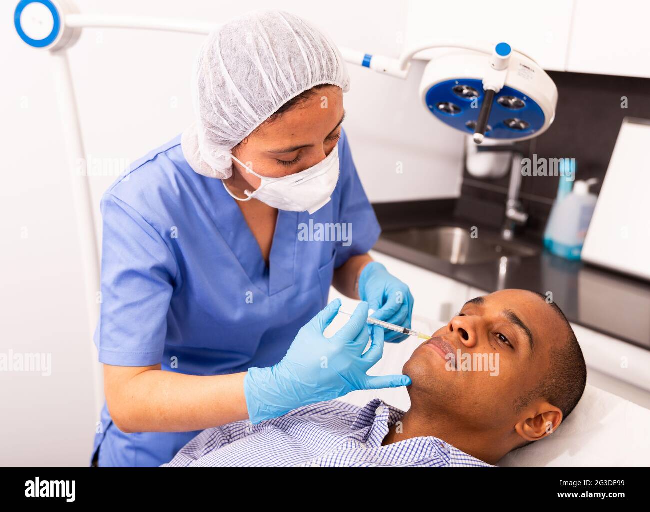 Female beautician injecting facial filler into skin for male client ...