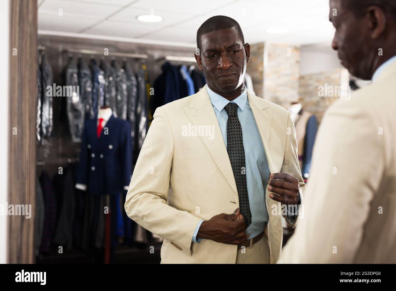 Confident male customer choosing fashion beige suit in mens store Stock ...