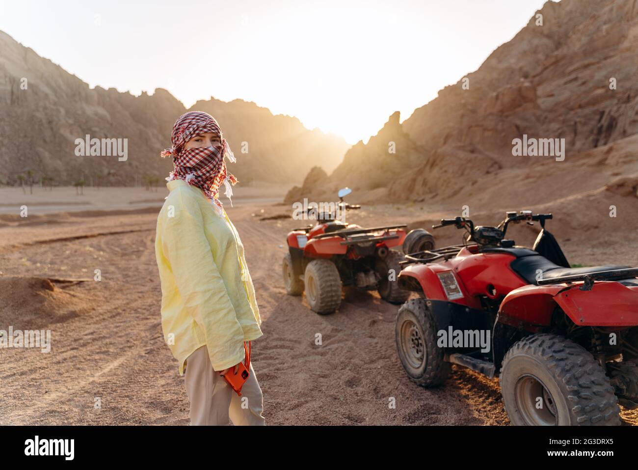 Young girl with a covered face preparing for a desert safari on ATVs. A ...