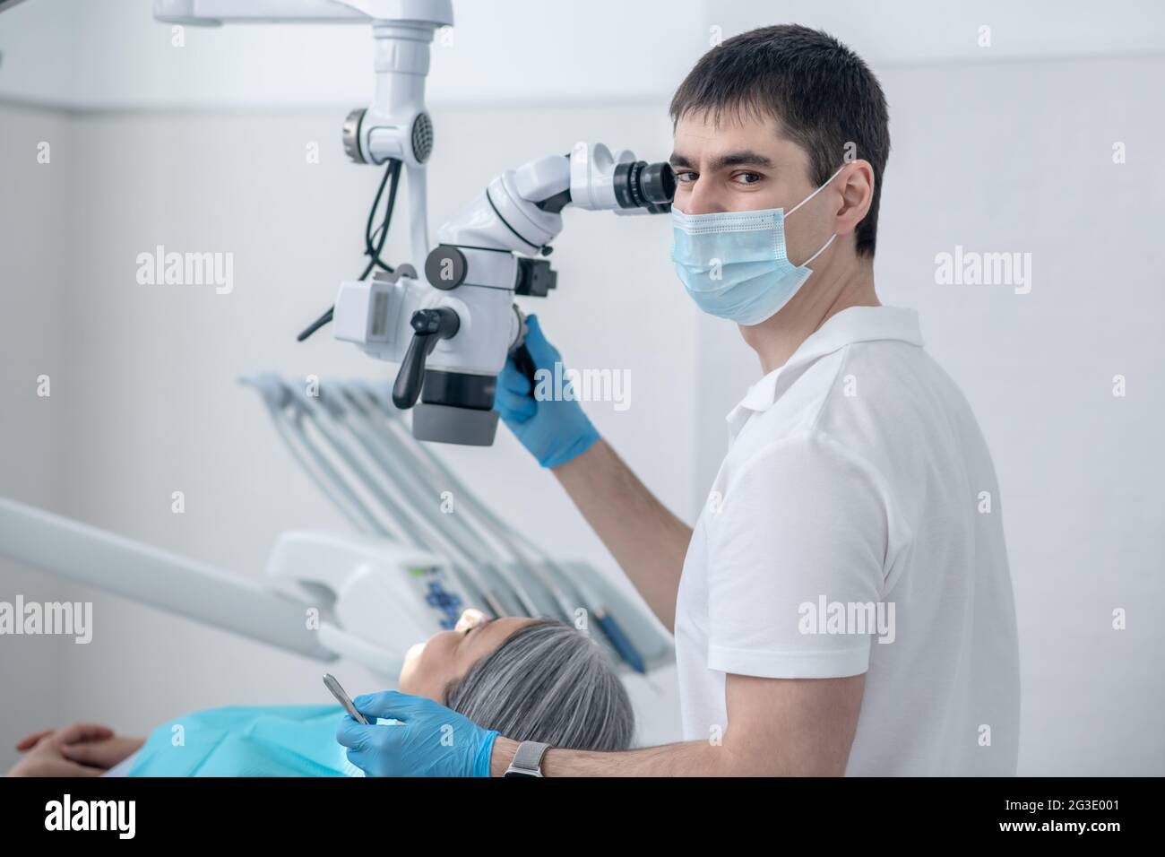 Male dentist working using optical medical instrument while doing a ...