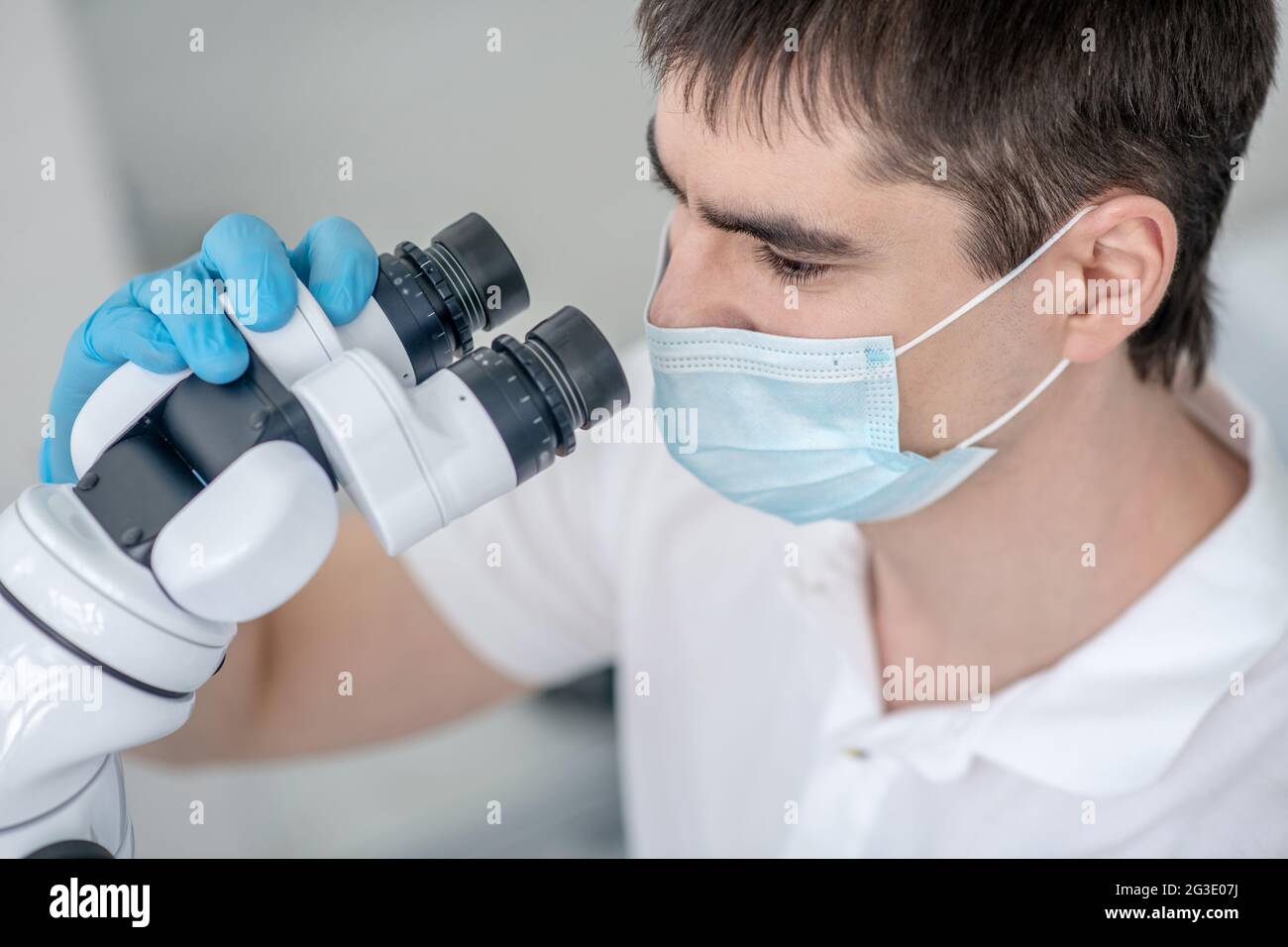 Male dentist working using optical medical instrument while doing a ...