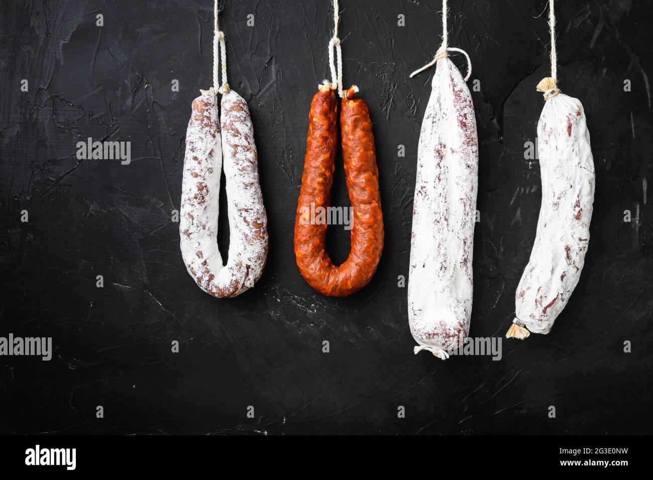 Spanish salami, fuet and salchichon sausages hang from a rack on black ...