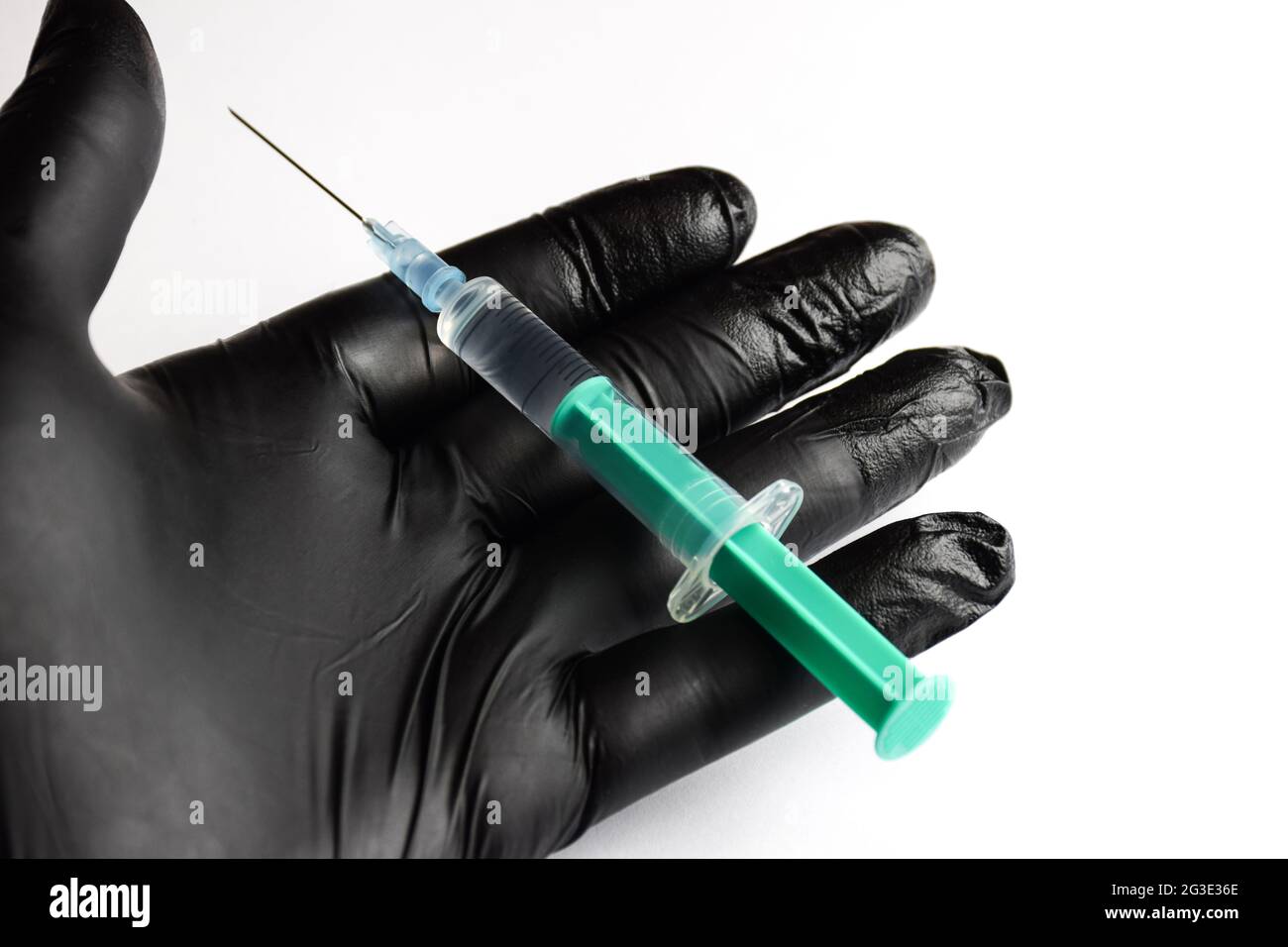 Hand in a black glove with a plastic syringe and a needle on a white ...