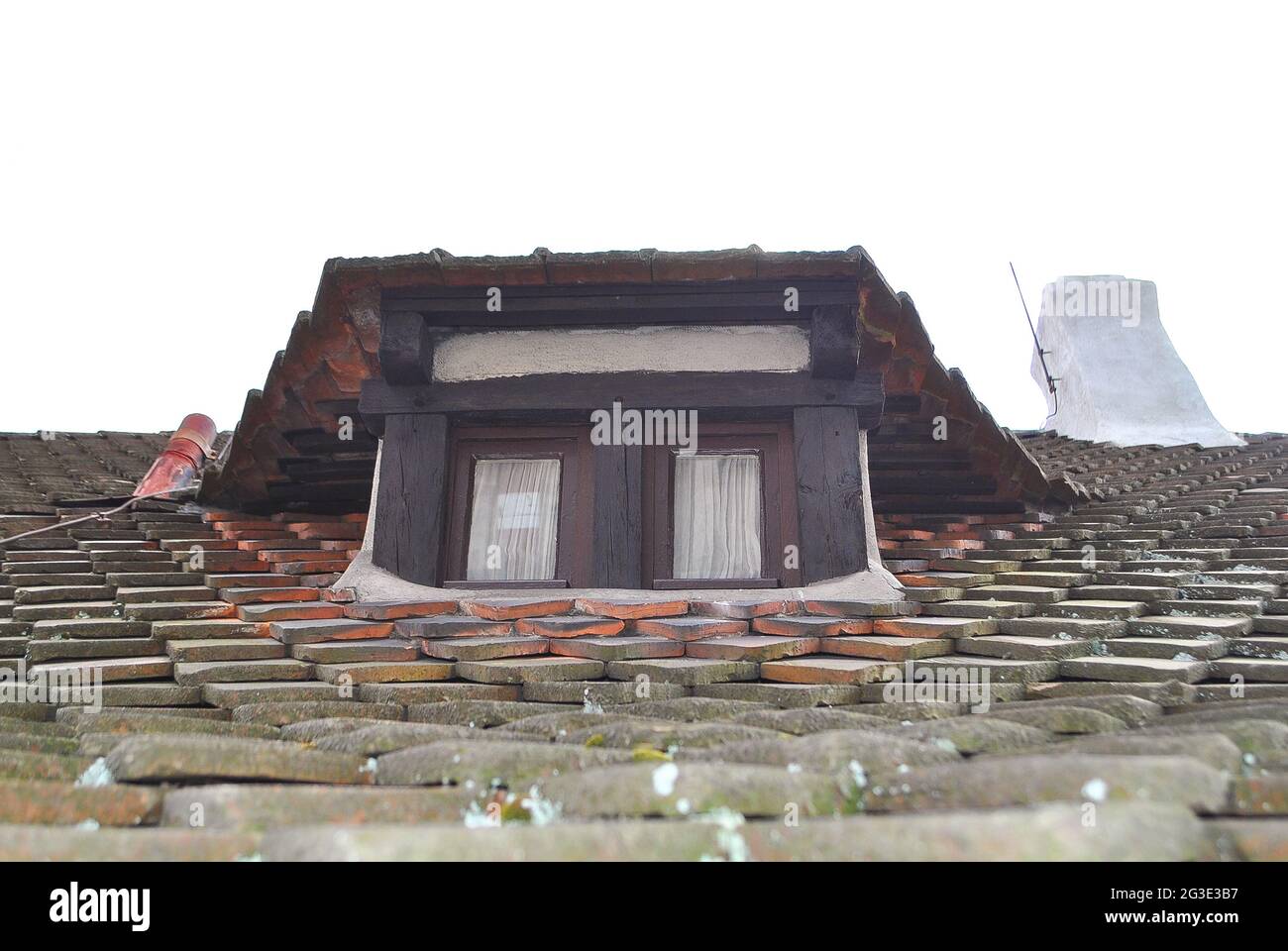 Small attic window on the tiled roof of an old building and chimney ...