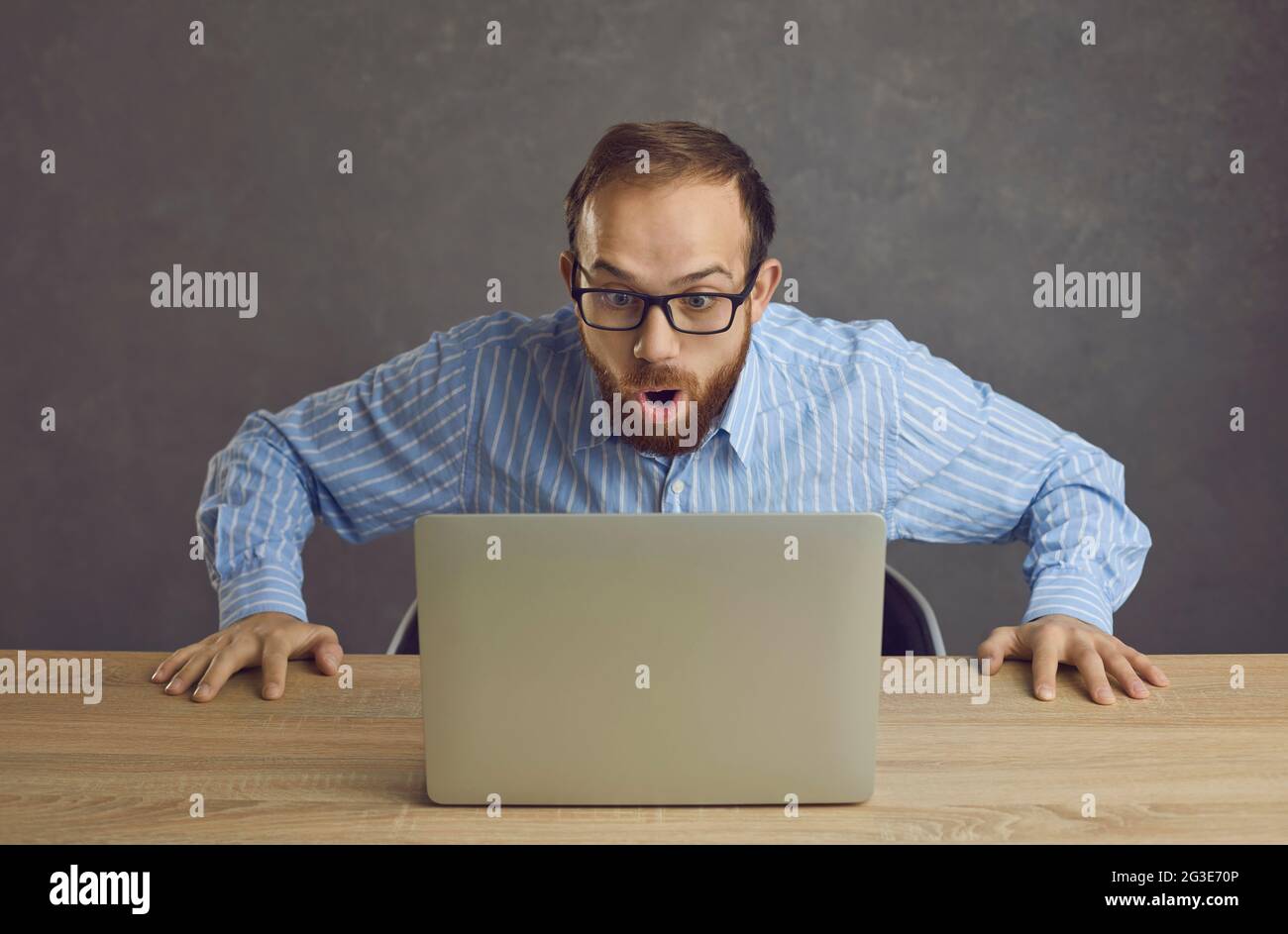 Shocked but happy man in glasses looking at laptop computer screen with ...
