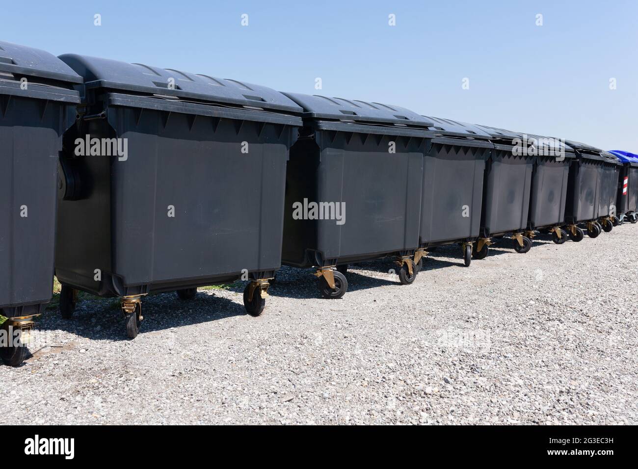 Diagonal row of black garbage containers on gravel outside under the ...
