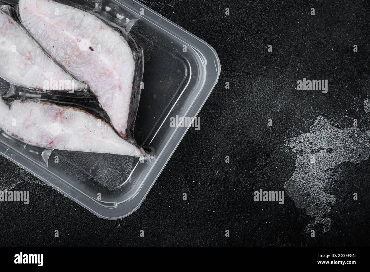 Halibut fish frozen steak pack set, on black dark stone table ...